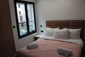 Quarto de hotel com cama, janela e mesa de cabeceira.