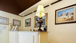 Uma mesa de recepção com certificados emoldurados, uma luminária e uma pintura de um edifício.