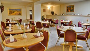 Uma sala de jantar de hotel com várias mesas redondas e cadeiras, dispostas em um espaço amplo.
