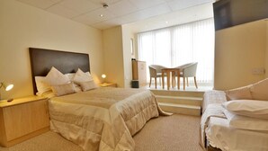 Quarto de hotel com uma cama grande, uma cama menor, uma escrivaninha e uma cadeira.