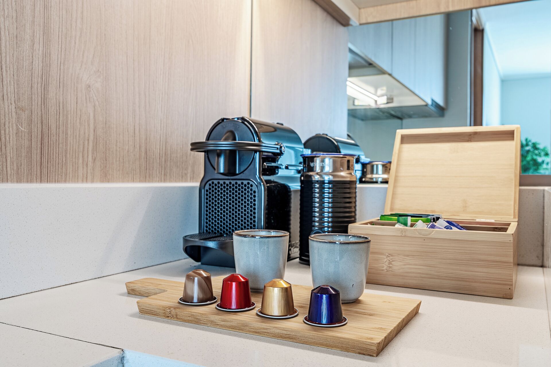 Uma bancada de cozinha com cafeteira, chaleiras e uma caixa de saquinhos de chá.