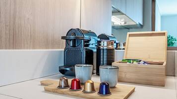 Uma bancada de cozinha com cafeteira, chaleiras e uma caixa de saquinhos de chá.