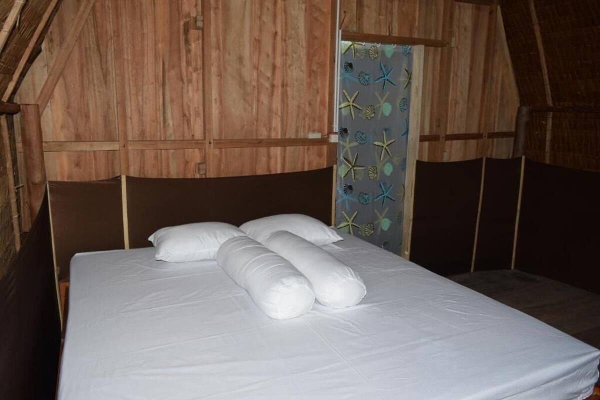 Uma cama de solteiro com roupa de cama e almofadas brancas, uma cabeceira de madeira e uma janela com cortina estampada com estrelas-do-mar.