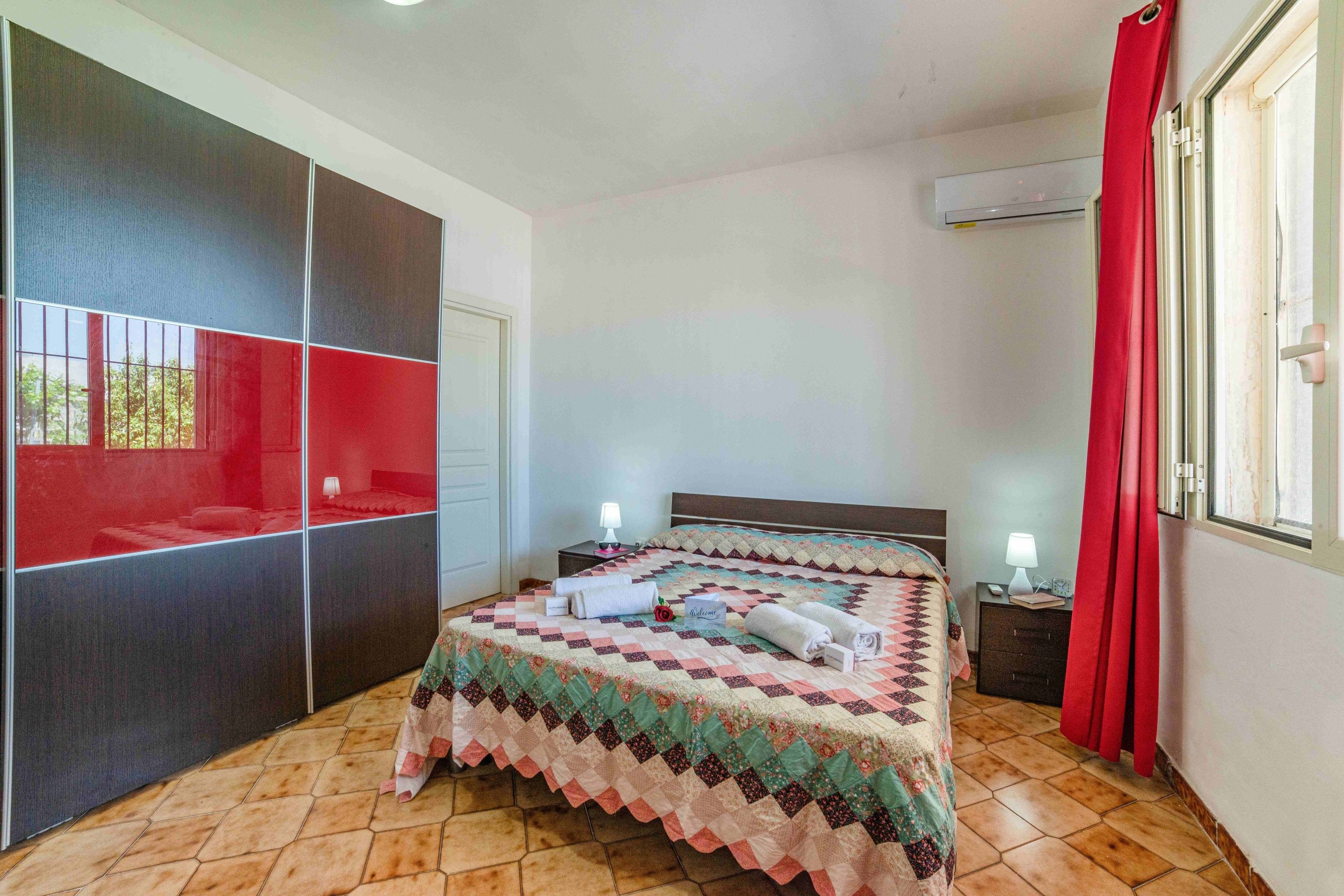 Um quarto com cama, mesa de cabeceira, guarda-roupa e janela com cortinas.