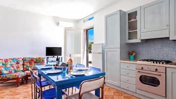 Cozinha moderna com área de refeições, apresentando uma mesa azul posta para dois, um sofá com padrão floral colorido e uma janela grande.