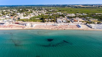 Vista aérea de uma cidade costeira com praia, edifícios e água azul cristalina.