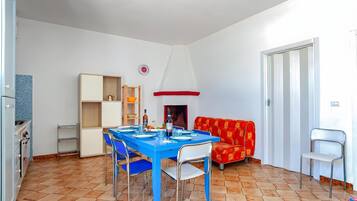 Uma área de refeições com mesa azul, cadeiras e sofá vermelho. Há também uma cozinha com armários e fogão.