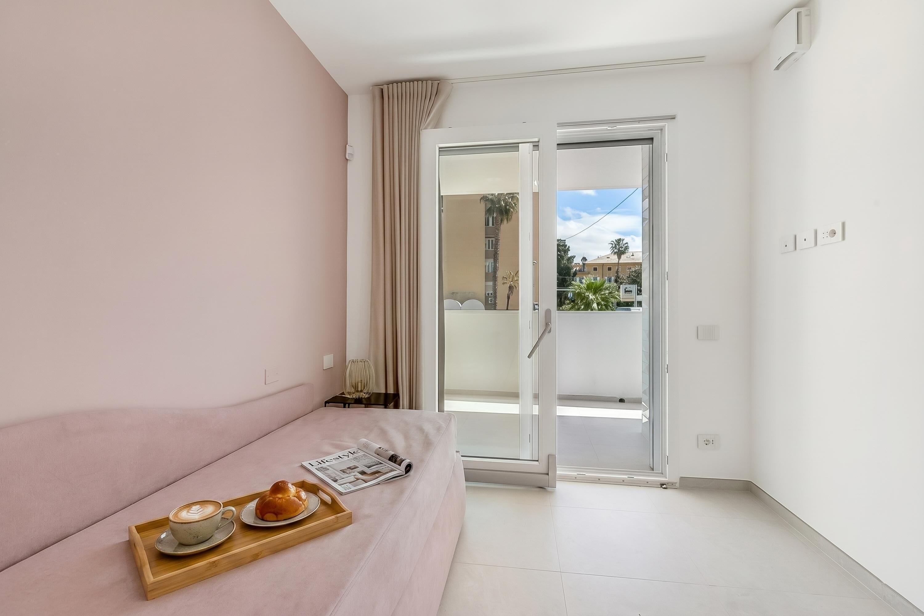 Quarto moderno com cama, bandeja com xícara e croissant, e porta que dá para uma varanda.