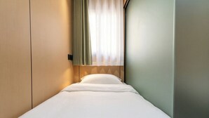 Uma cama de solteiro com roupa de cama branca em um quarto de hotel.