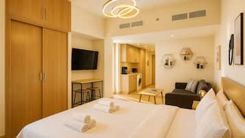 Quarto de hotel com uma cama grande, televisão, pequena cozinha e área de estar com sofá.
