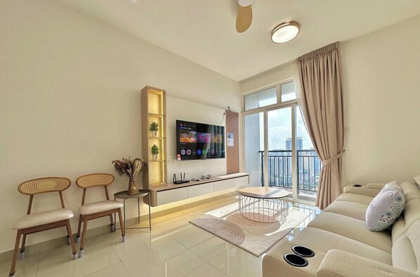 Uma sala de estar moderna com sofá, duas poltronas, mesa de centro, televisão e varanda com cortinas.