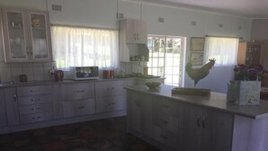Uma cozinha com armários, micro-ondas, pia e janela com cortinas.