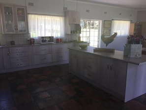Uma cozinha com armários, micro-ondas, pia e janela com cortinas.