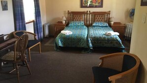 Quarto de hotel com duas camas, uma cadeira, uma mesa e um quadro na parede.