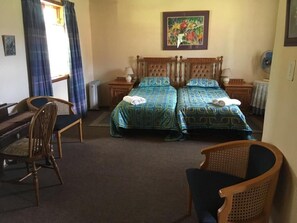 Quarto de hotel com duas camas, uma cadeira, uma mesa e um quadro na parede.
