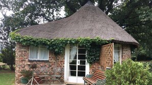 Uma cabana com telhado de palha e fachada de tijolos, uma porta e um banco na frente.