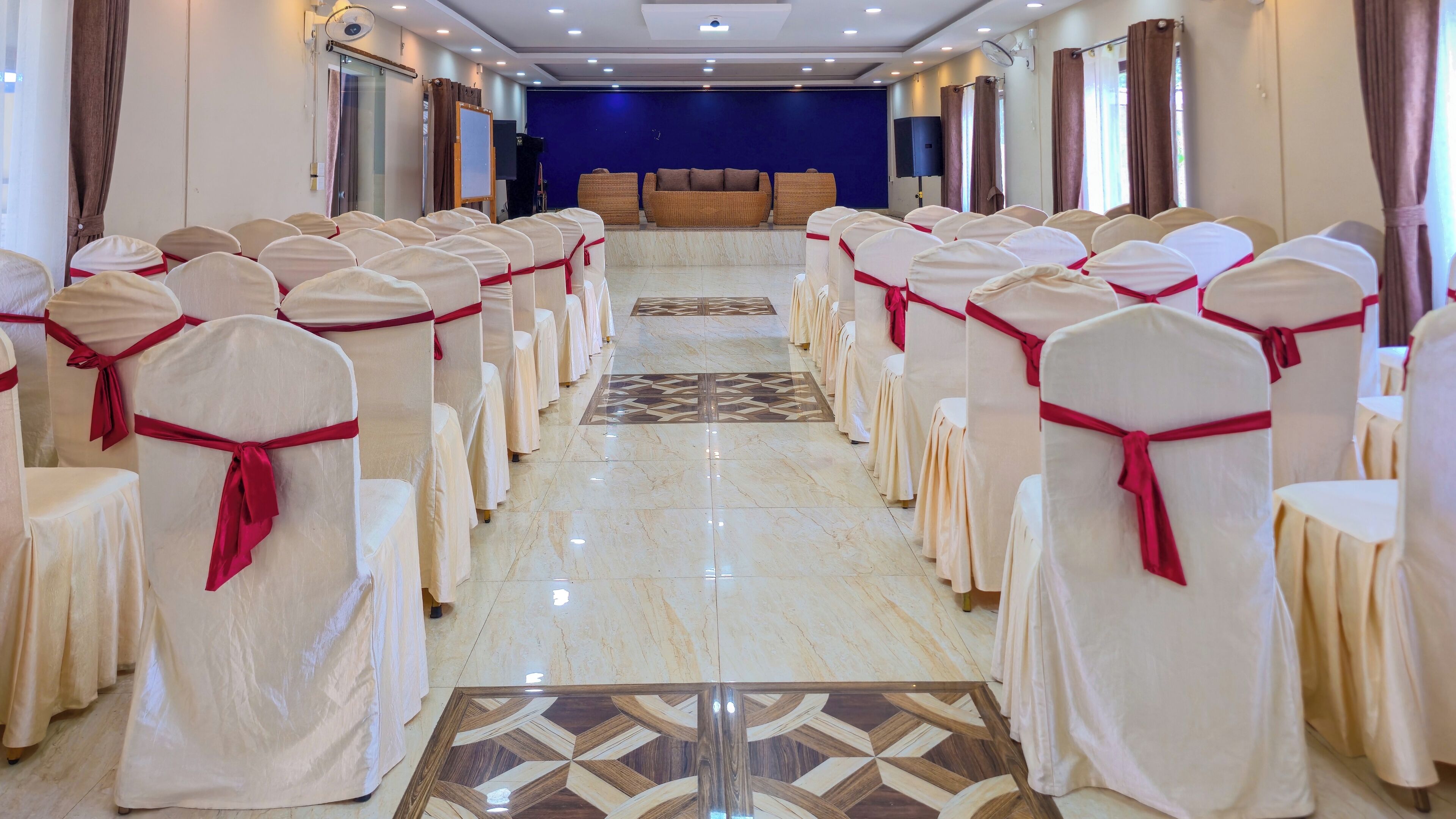 Uma sala de conferências de hotel com fileiras de cadeiras e mesas, um palco e uma parede azul.