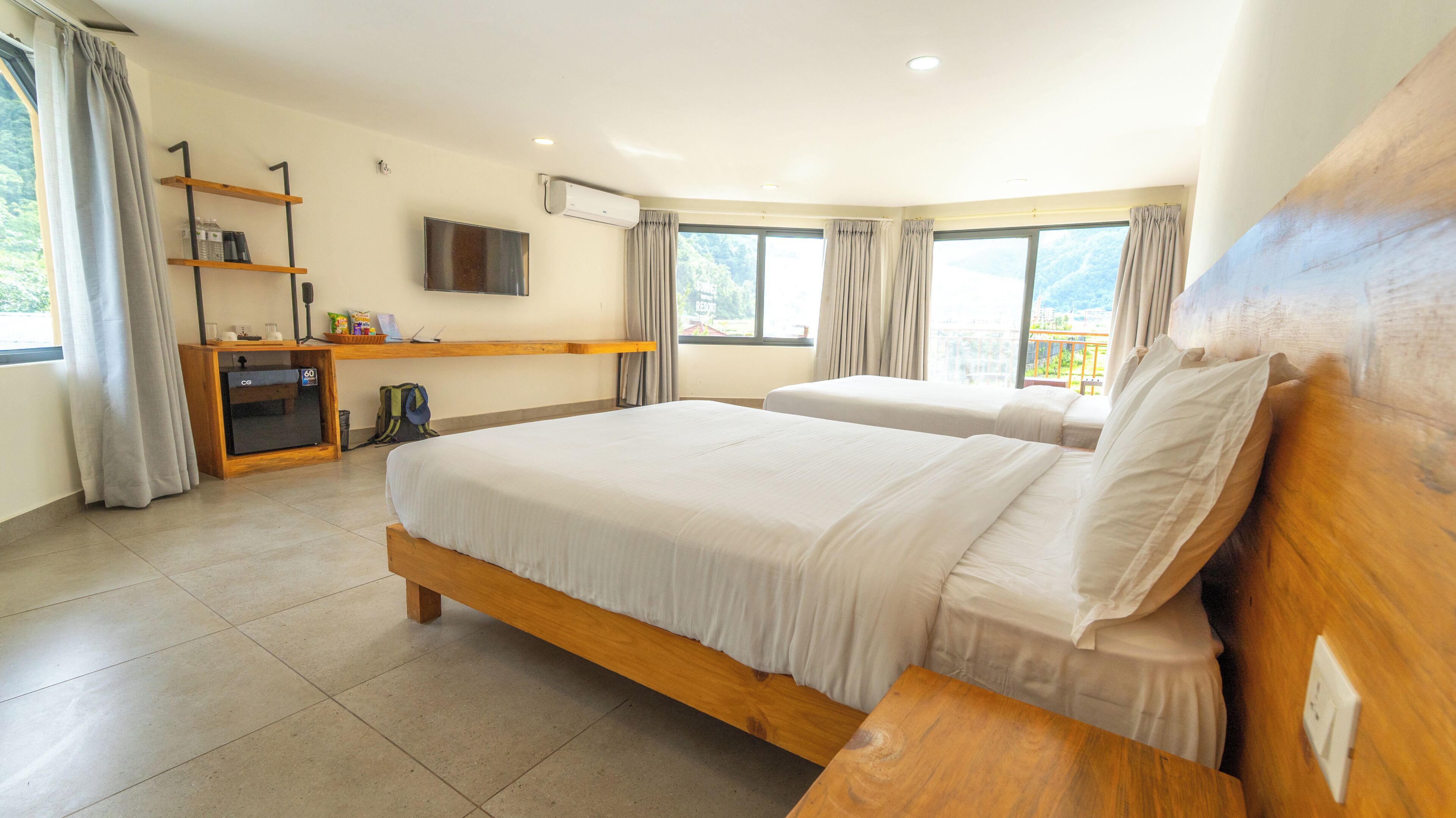 Quarto de hotel com uma cama grande, uma escrivaninha com cadeira, televisão e varanda com cortinas.