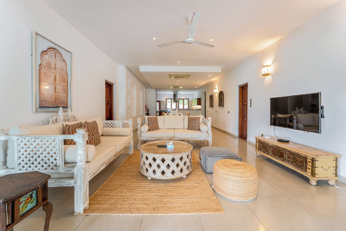 Uma sala de estar ampla com sofá, mesa de centro, TV e um aparador decorativo.