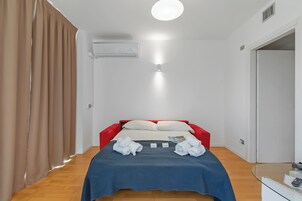 Quarto de hotel com uma cama, uma cadeira vermelha, uma mesa de vidro e uma porta.