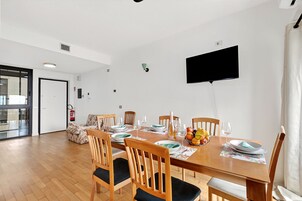 Uma sala de jantar com uma mesa de madeira posta para seis pessoas, rodeada por cadeiras de madeira com almofadas pretas.