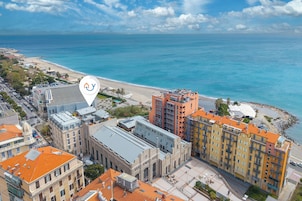 Paisagem costeira urbana com um hotel na praia, incluindo um edifício grande com telhado plano e uma estrutura menor com cúpula.