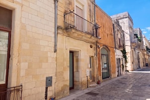 Uma rua estreita com edifícios de arquitetura tradicional, incluindo uma varanda com grade de metal.