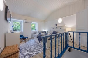 Quarto moderno com uma cama grande, uma escrivaninha e uma cadeira. Há uma janela com vista para o verde lá fora.