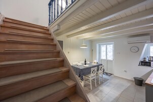 Uma escada leva a uma sala de jantar com uma mesa posta para quatro pessoas, um relógio na parede e um micro-ondas sobre um balcão.