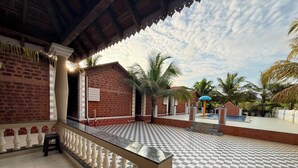 Uma área externa coberta com piso xadrez, piscina e palmeiras.