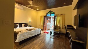 Quarto de hotel com cama, televisão, ventoinha no teto e vista para o exterior.
