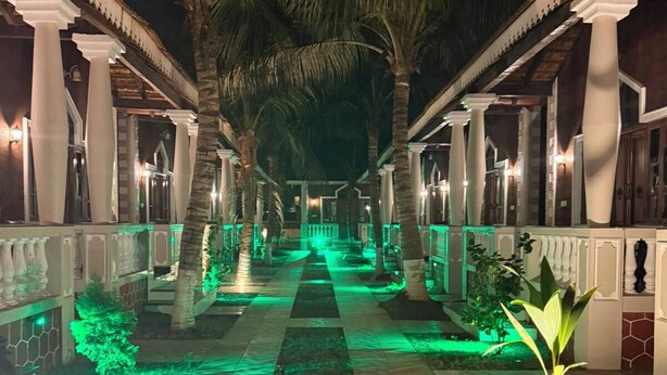 Uma trilha bordeada por palmeiras e colunas, conduzindo a um edifício com estilo arquitetônico tradicional.