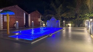 Uma piscina com iluminação azul, um edifício de tijolos e palmeiras.