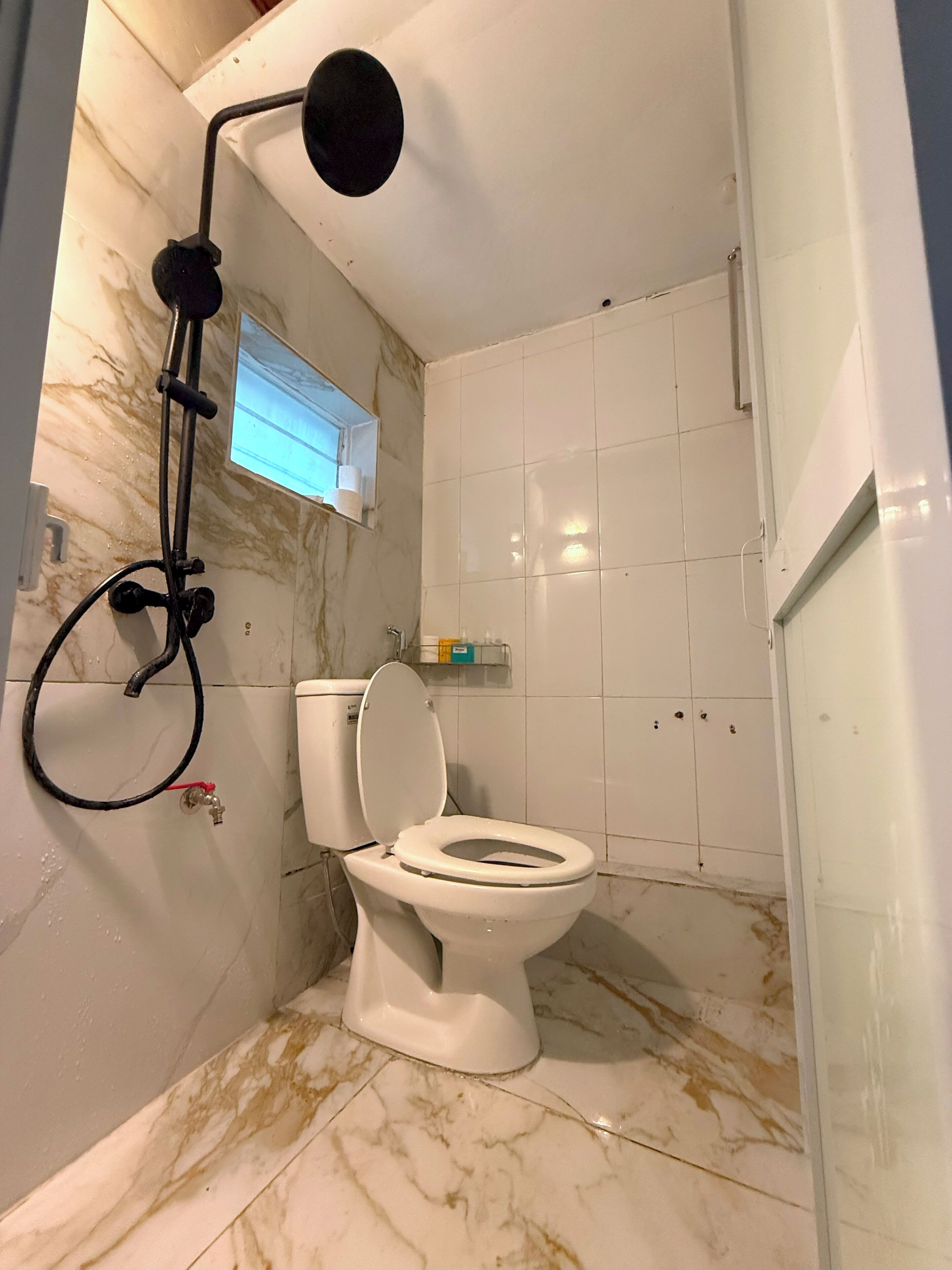 Casa de banho com sanita, chuveiro e soalho em mármore.