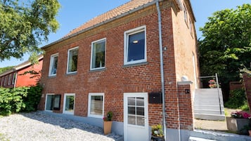 Um edifício de tijolos vermelhos com porta e janelas brancas e um caminho de acesso de brita.