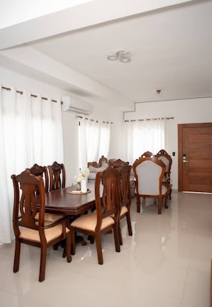 Uma sala de jantar com uma mesa de madeira redonda, seis cadeiras e um vaso com flores.