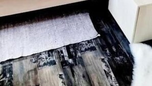 Uma cama com almofadas, uma pequena mesa de cabeceira com uma planta, e uma janela com cortinas amarelas.