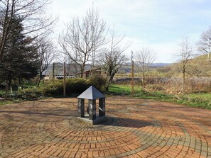 Uma área circular pavimentada com um monumento central com telhado triangular e inscrições.