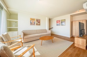 Uma sala de estar com sofá, mesa de centro, cadeiras de madeira e um rack para TV.