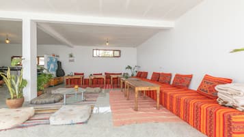Uma sala de estar ampla com sofás, uma mesa de jantar e uma cozinha ao fundo.