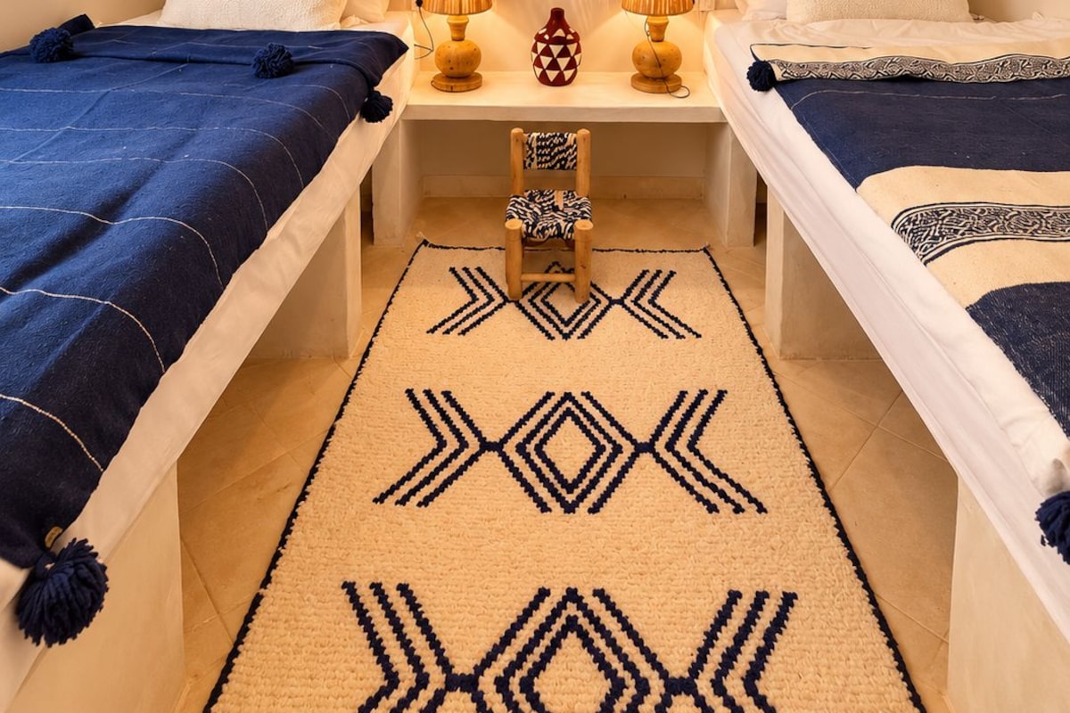 Quarto com duas camas, uma mesa central com luminárias, um vaso decorativo e duas obras de arte nas paredes.