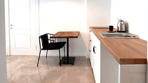 Uma cozinha compacta com bancada de madeira, uma cadeira preta, uma luminária pendente e uma porta branca.