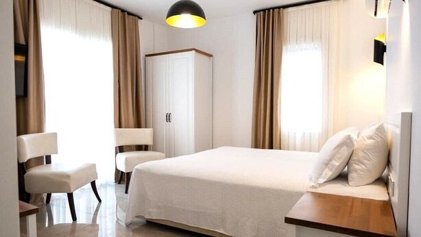 Quarto de hotel com cama, cadeira, guarda-roupa e mesa de cabeceira.
