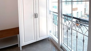 Quarto com uma janela grande, guarda-roupa branco e varanda com grade de metal.
