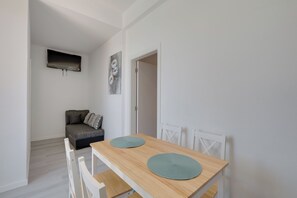 Uma sala de jantar com mesa de madeira, duas cadeiras brancas e um sofá cinza com almofadas.