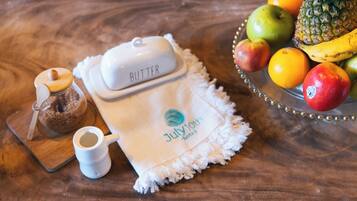 Uma mesa de madeira com um pote de geleia, uma xícara branca pequena, um recipiente para manteiga e um prato com frutas.