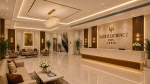 Um saguão de hotel com balcão de recepção, sofás, um lustre e uma escadaria.