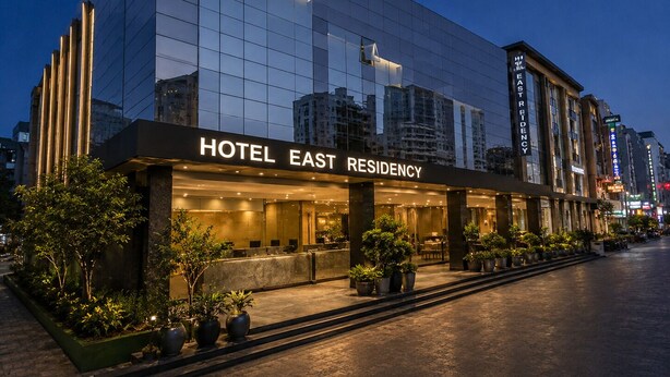 Um edifício moderno de hotel com fachada de vidro e uma placa com a inscrição 'HOTEL EAST RESIDENCY'.