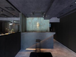 Uma área de recepção moderna, com parede de concreto, balcão de vidro e escada para um andar superior.