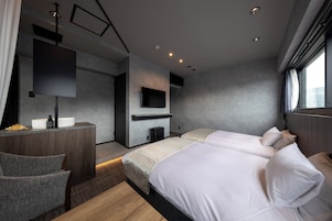 Quarto de hotel moderno com televisão de tela plana, escrivaninha com cadeira, cama com roupa de cama branca e janela com cortinas.